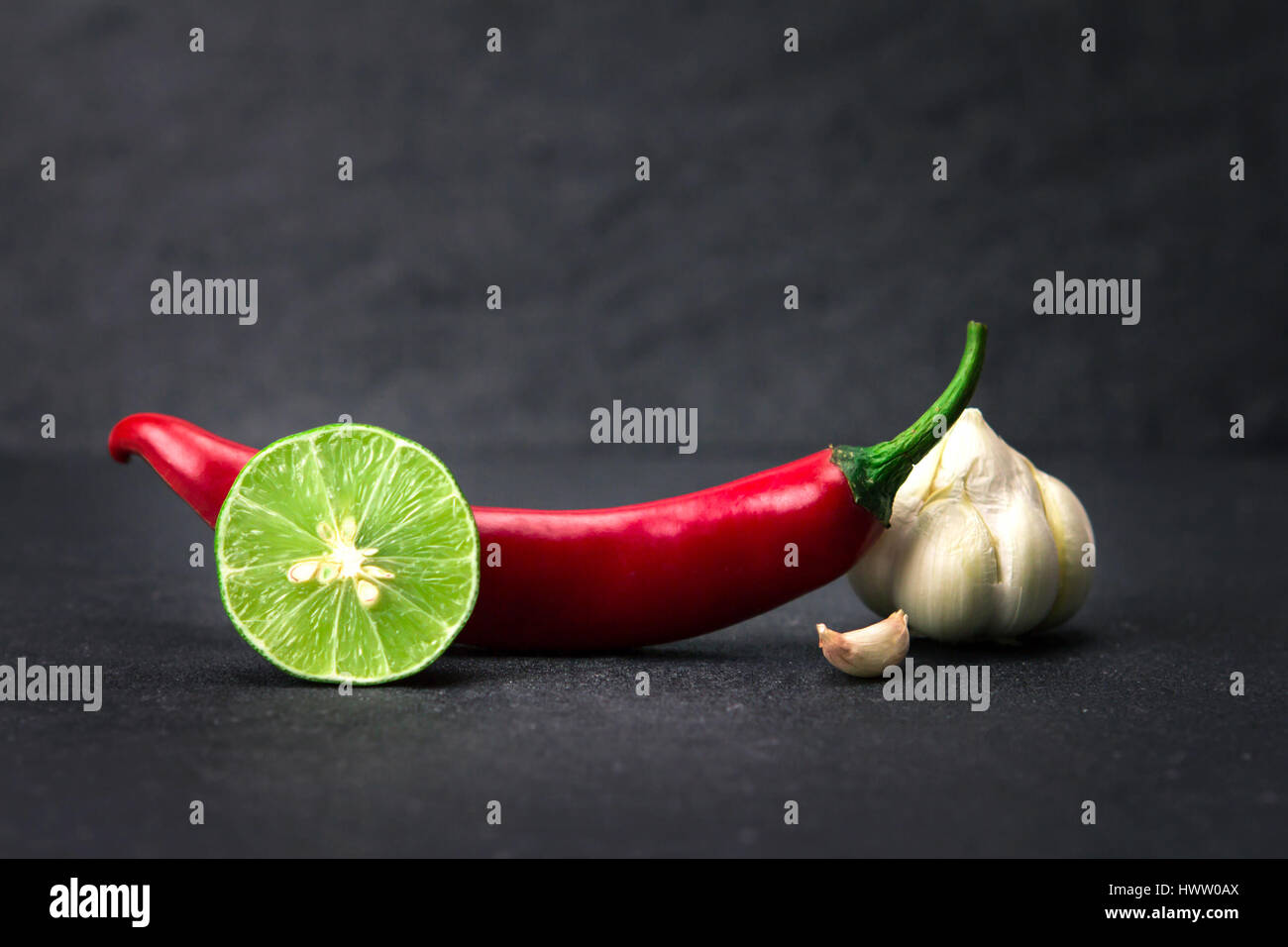 red chili , garlic and lime lemon arrange on black stone background ...