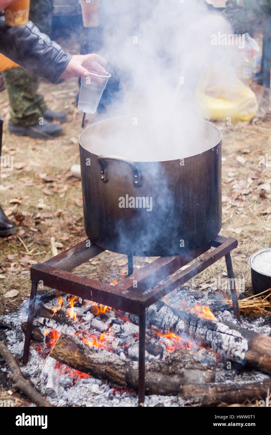 metal pot with a meal basking on burning firewood in the forest ...