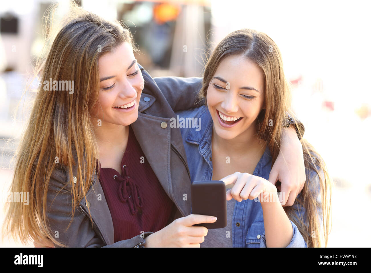 Two happy affectionate friends sharing a smart phone watching ...