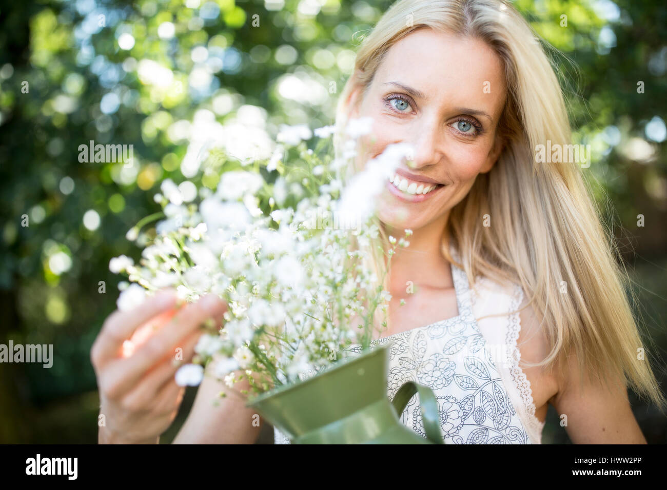 Smiling woman holding jug with flowers outdoors Stock Photo - Alamy