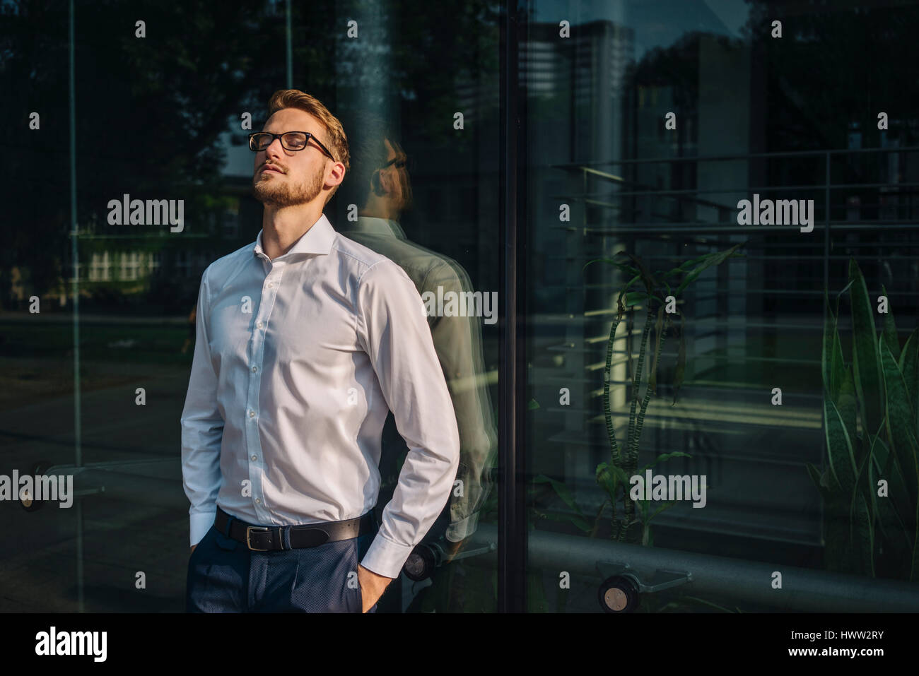 Businessman leaning against glass wall Stock Photo - Alamy