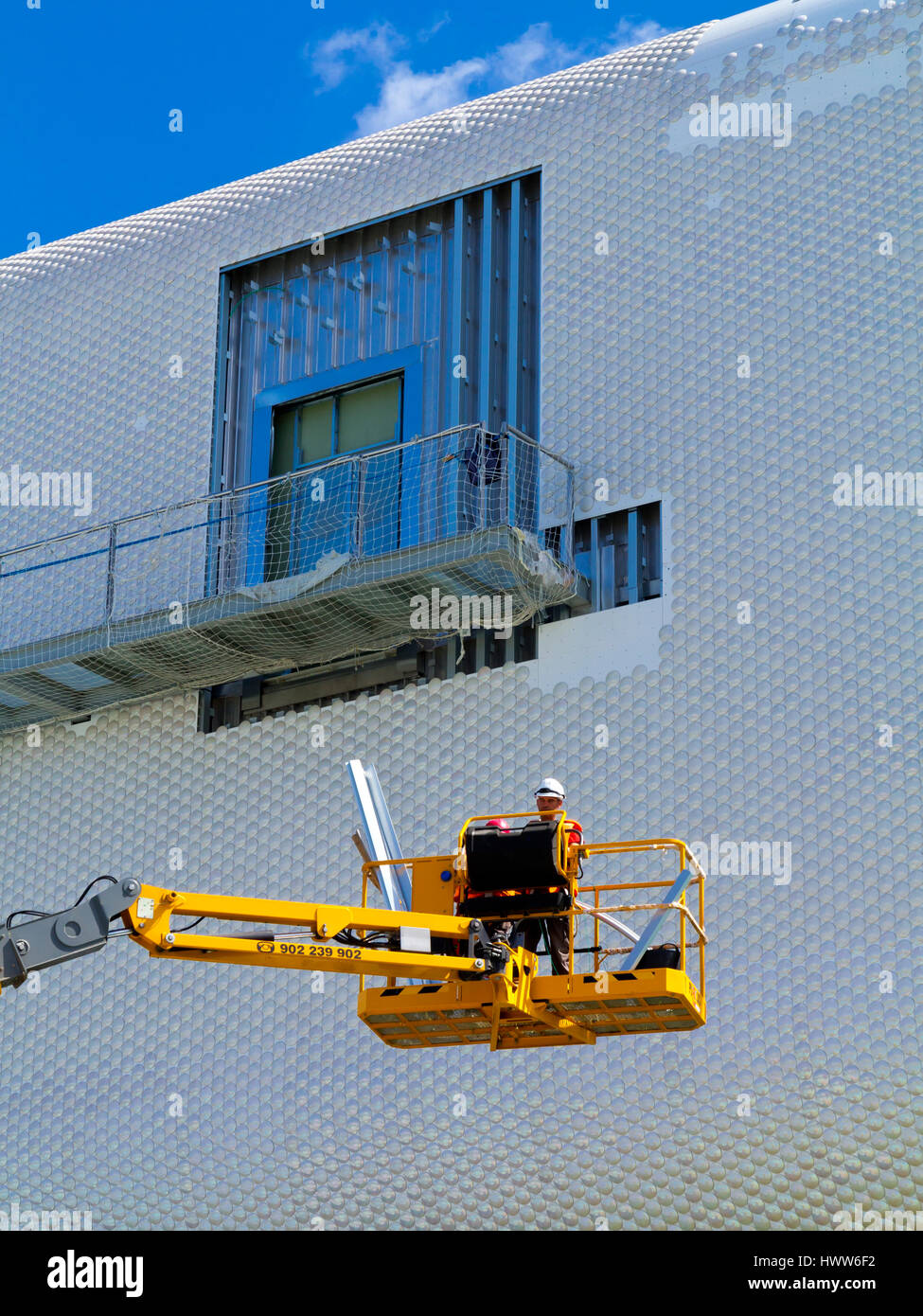 Workman using a cherry picker to repair the side of a modern building ...