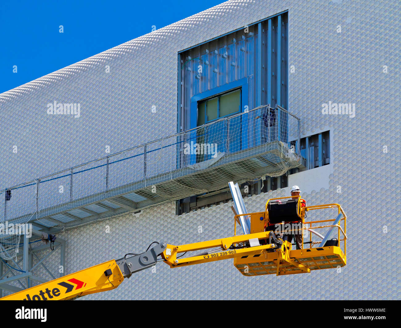 Workman using a cherry picker to repair the side of a modern building ...