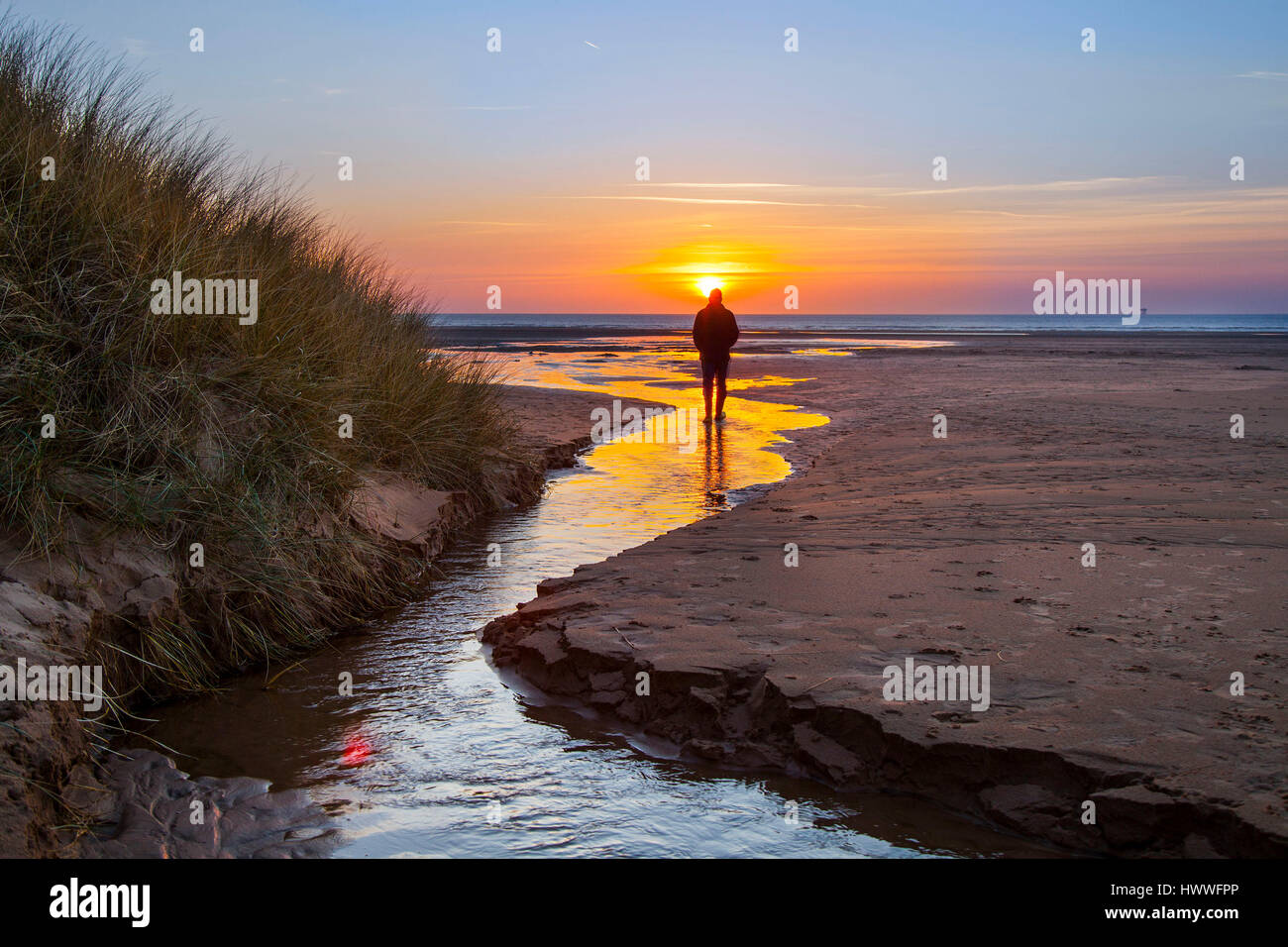 A rivulet of water trickles to sea as the sunsets in Southport ...