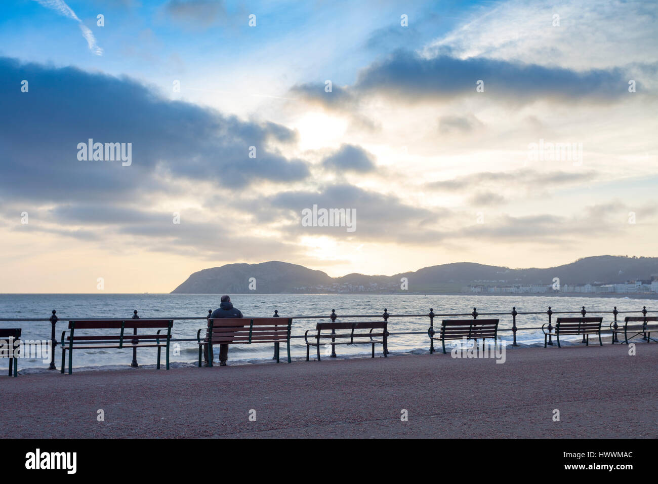A silhouetted man sitting on a promenade bench watching the sunrise ...