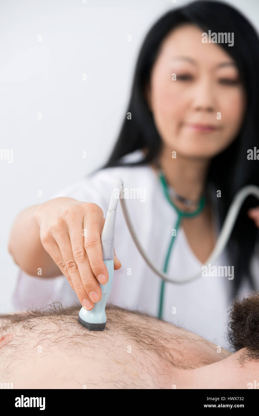Female doctor placing ultrasound probe on male patient's chest in ...