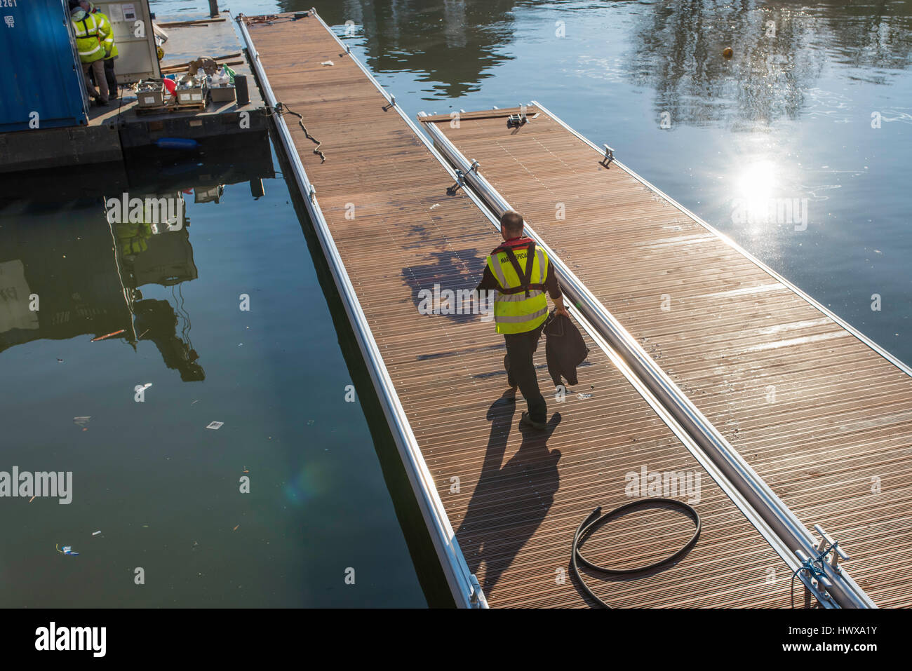 A manual worker walking across a jetty floating on water to join his ...