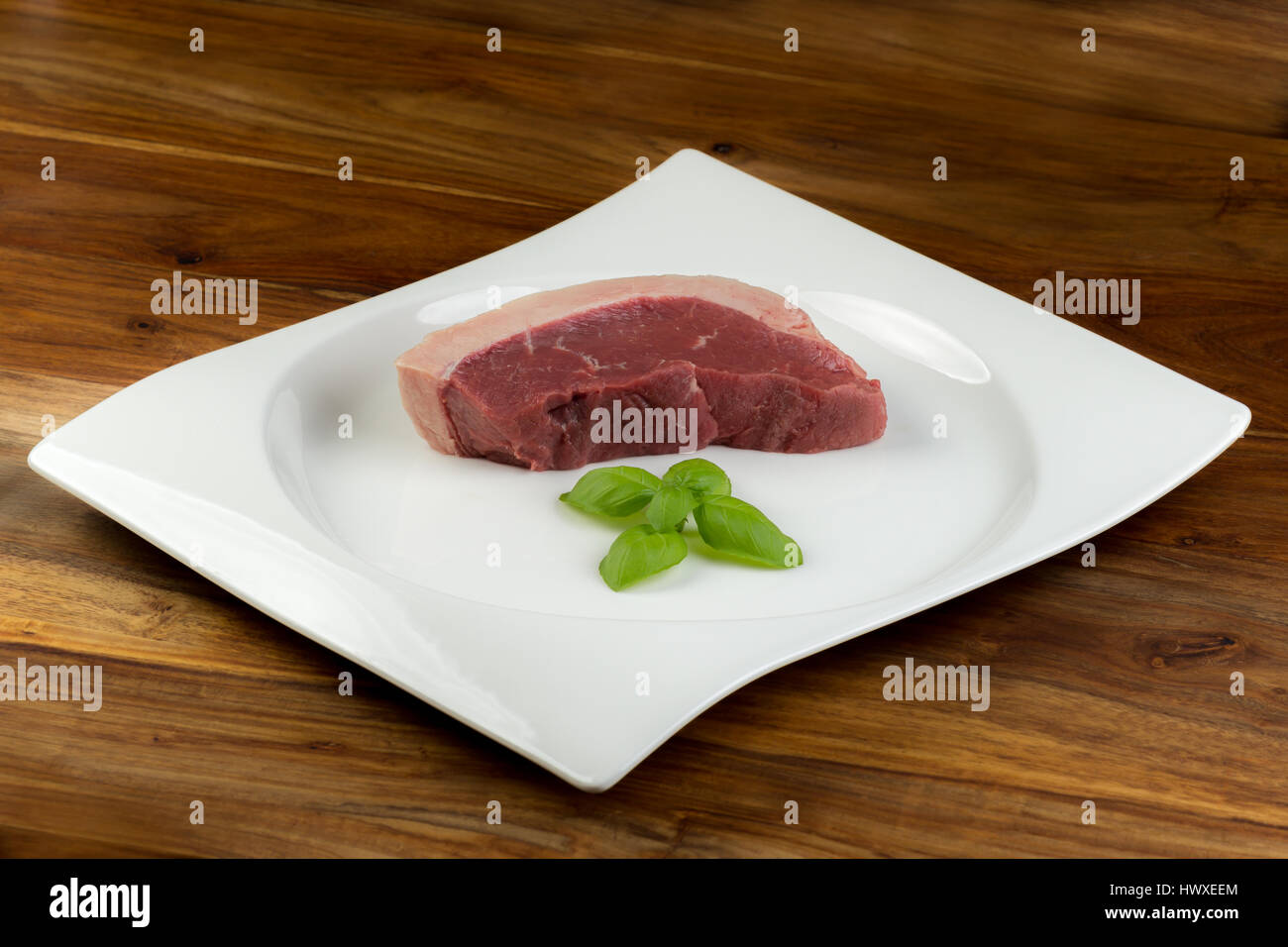 Slice of fresh raw cow beef (picanha) and basil leaves on a white dish ...