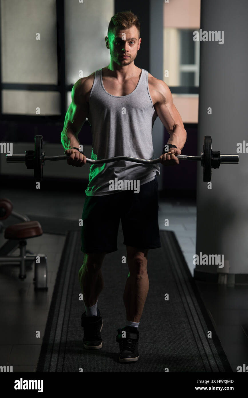 Muscular Man Doing Heavy Weight Exercise For Biceps With Barbell In Gym ...