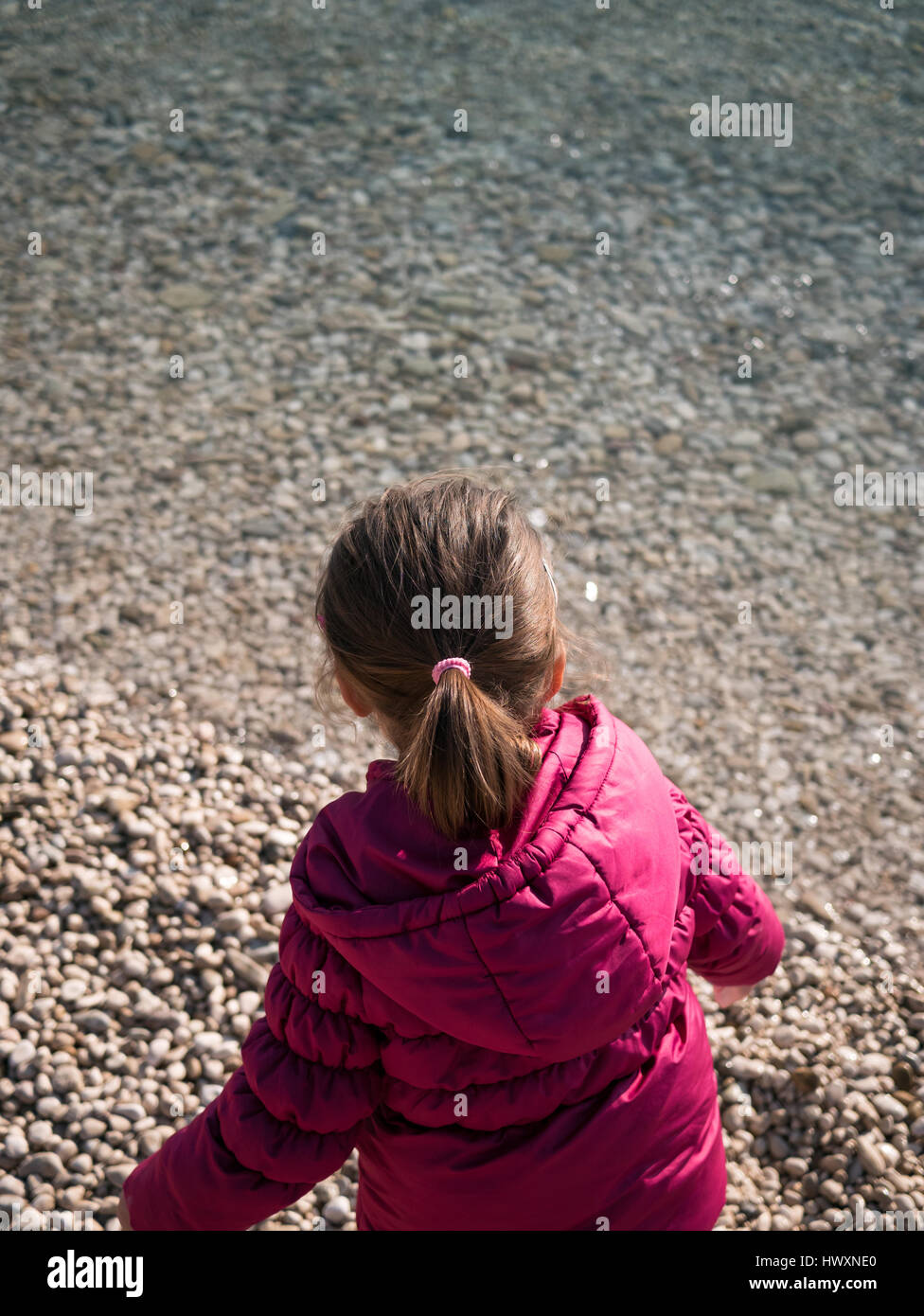 Little girl on the pebble beach near calm crystal clear sea back view ...