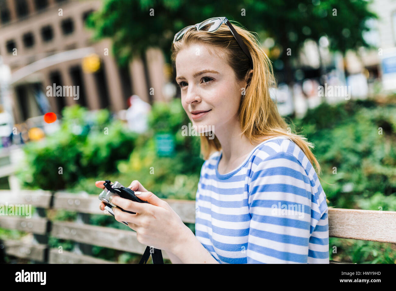 Young woman sitting on bench, holding camera Stock Photo - Alamy