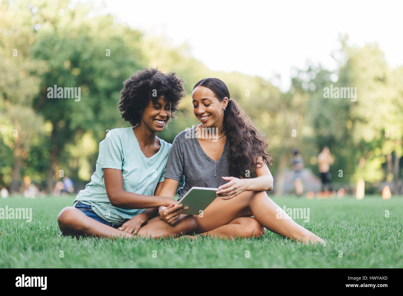 Two best friends sitting on a meadow of a park having fun with mini ...