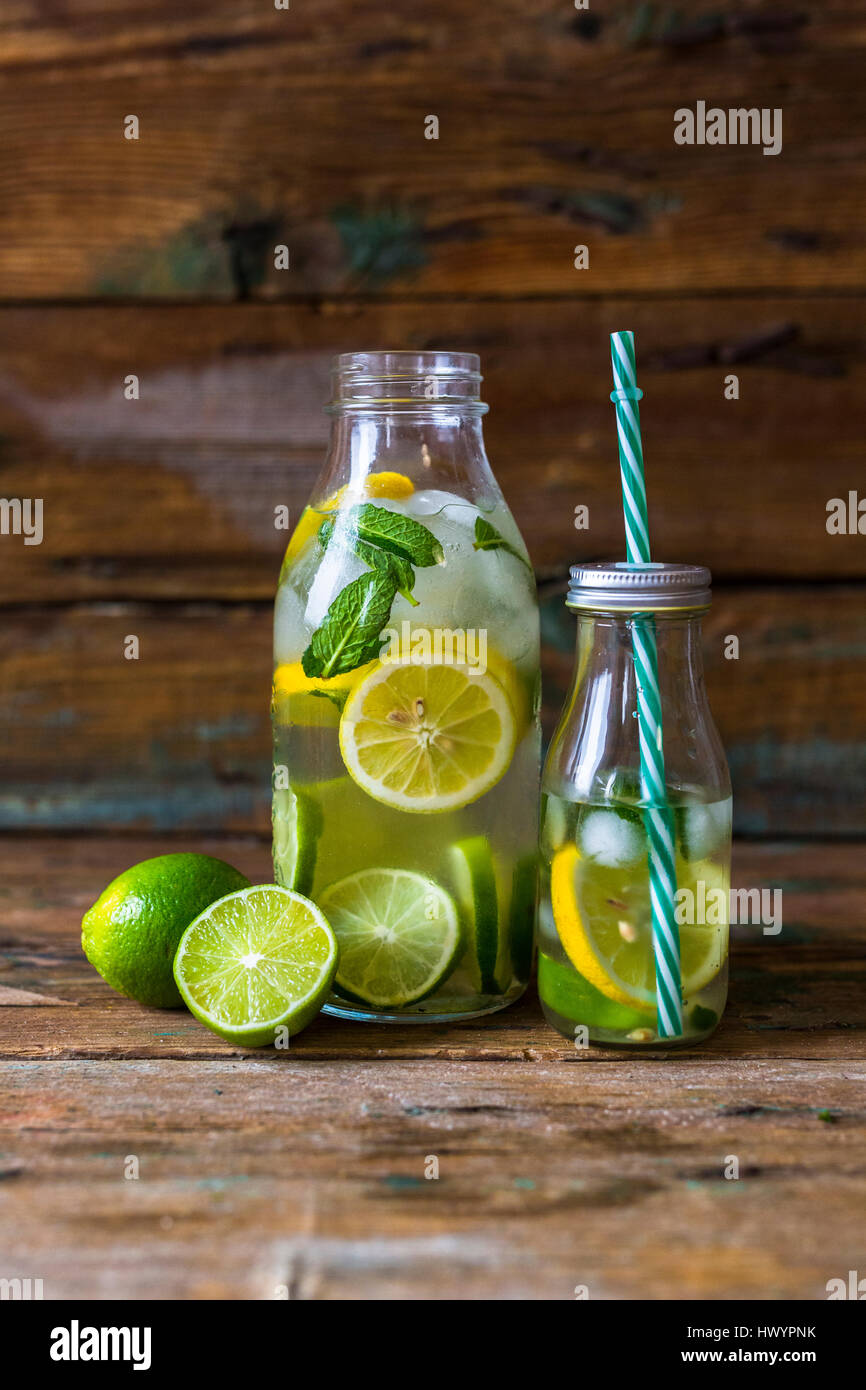 Glass bottles of infused water with lemon, lime, mint leaves and ice ...