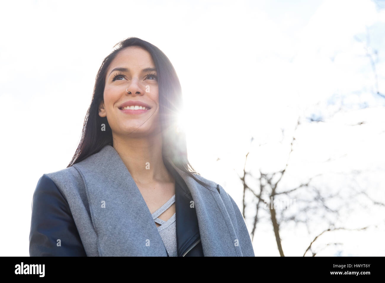 Portrait of smiling young woman with nose piercing at backlight looking ...