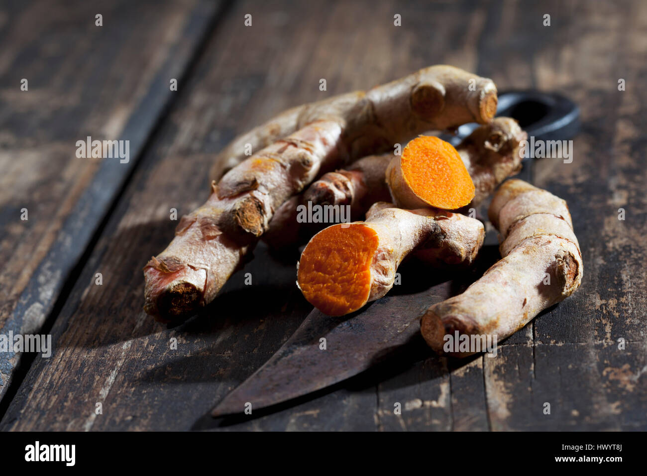 Whole and sliced turmeric and an old knife on dark wood Stock Photo - Alamy