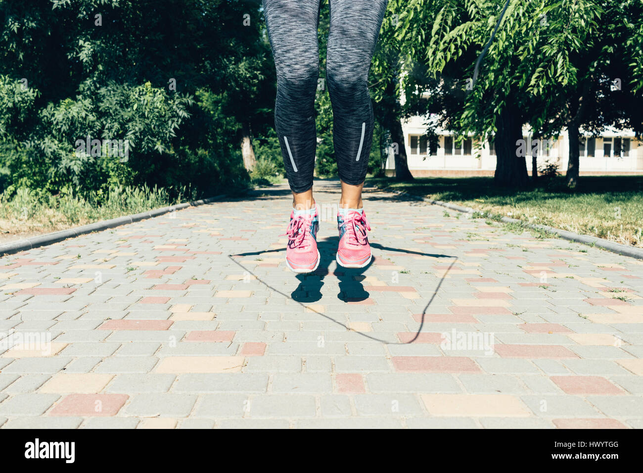Close-up of female legs in sneakers jumping rope in summer outdoors ...