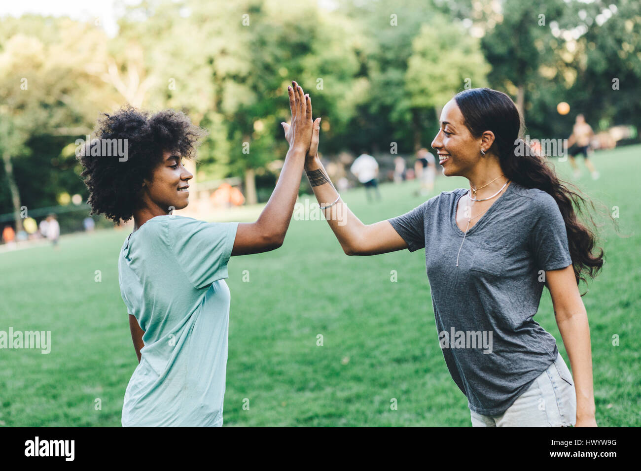 Two young woman high fiving in a park Stock Photo - Alamy
