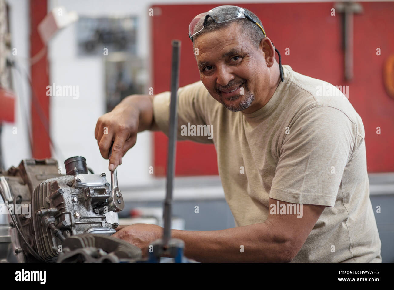 Smiling mechanic working on motorcycle engine in workshop Stock Photo ...
