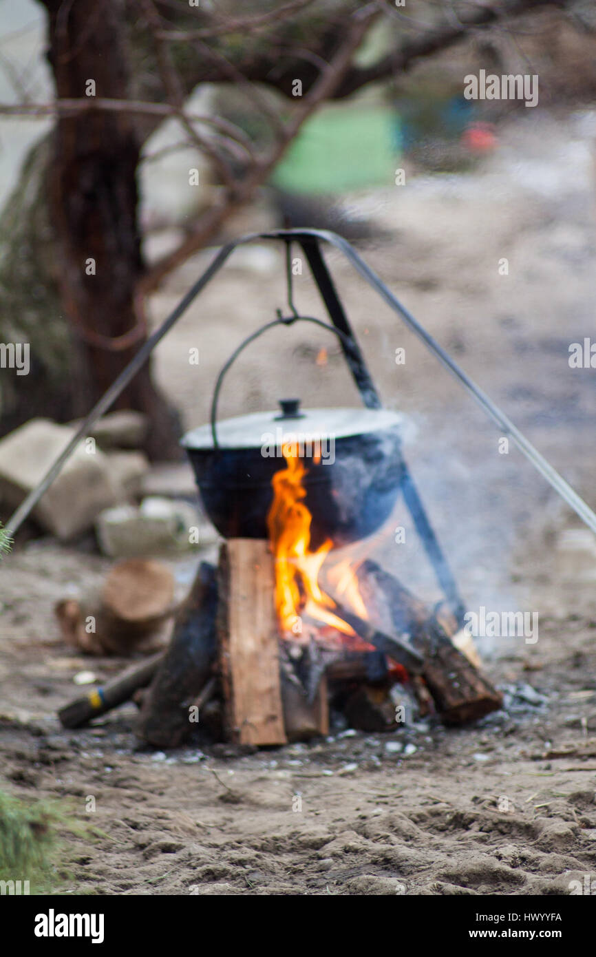 metal pot with a meal basking blured on burning firewood in the forest ...
