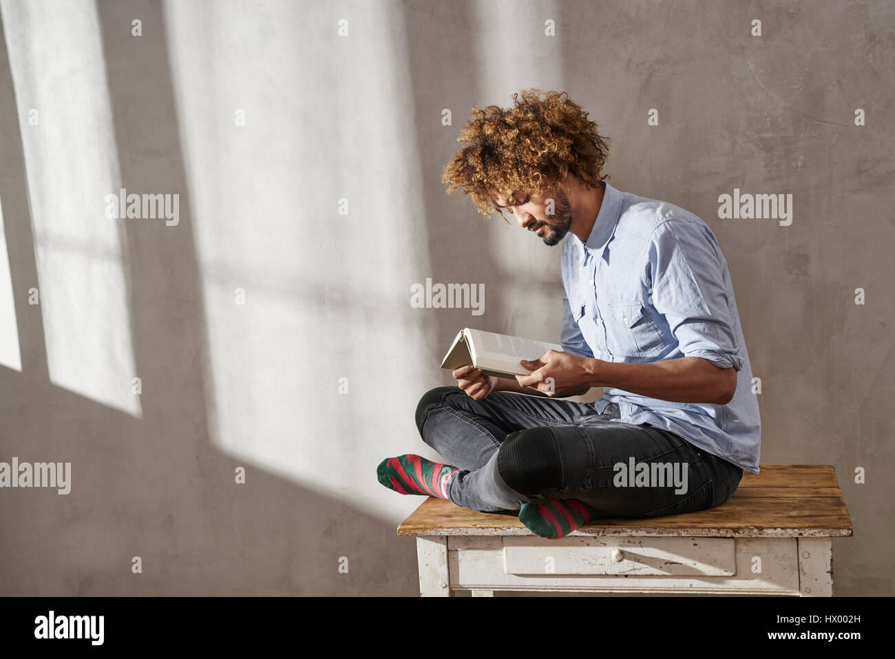 Young man sitting on wooden table reading book Stock Photo - Alamy