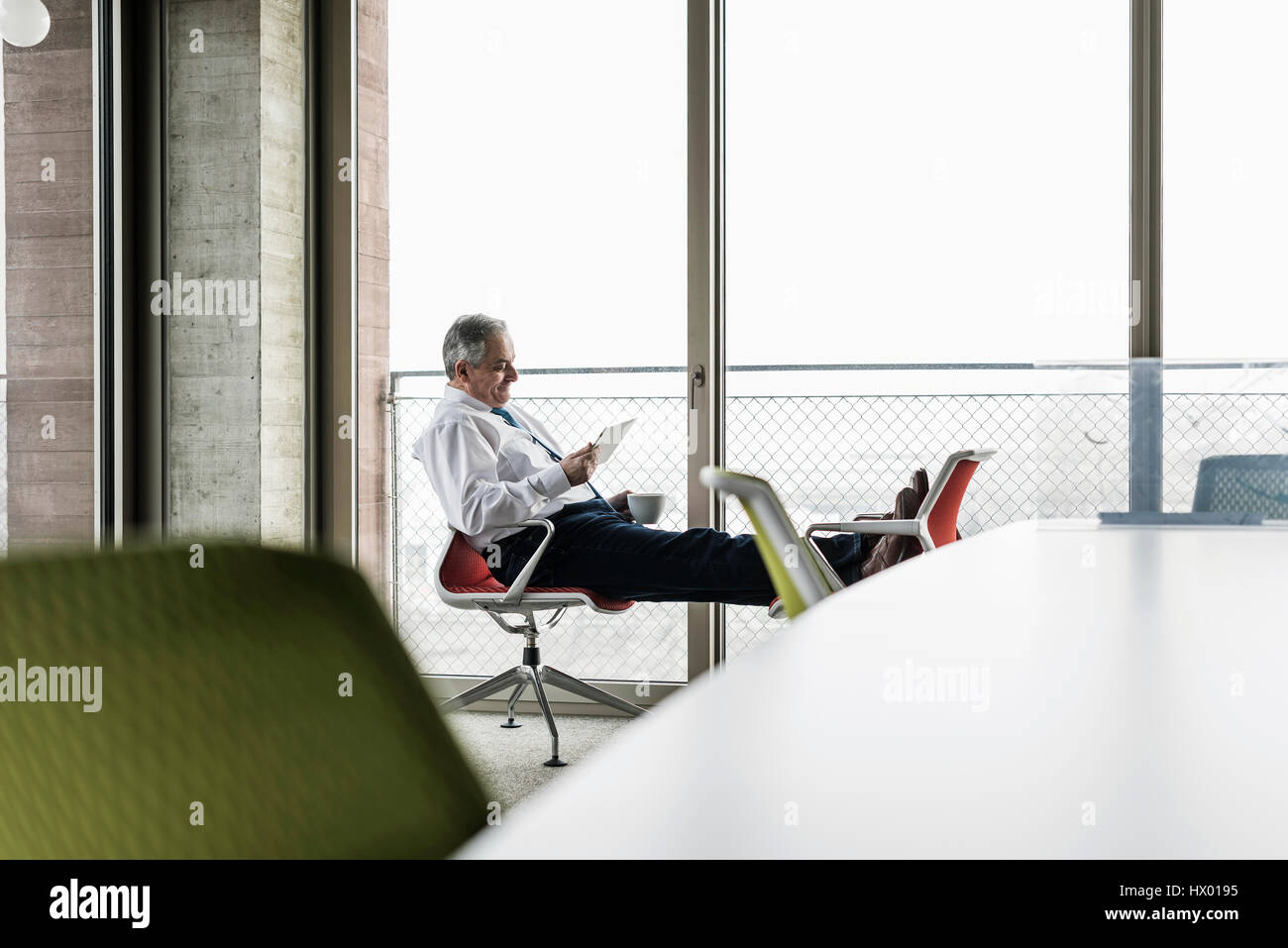 Senior manager in office sitting on chairs with feet up using digital ...