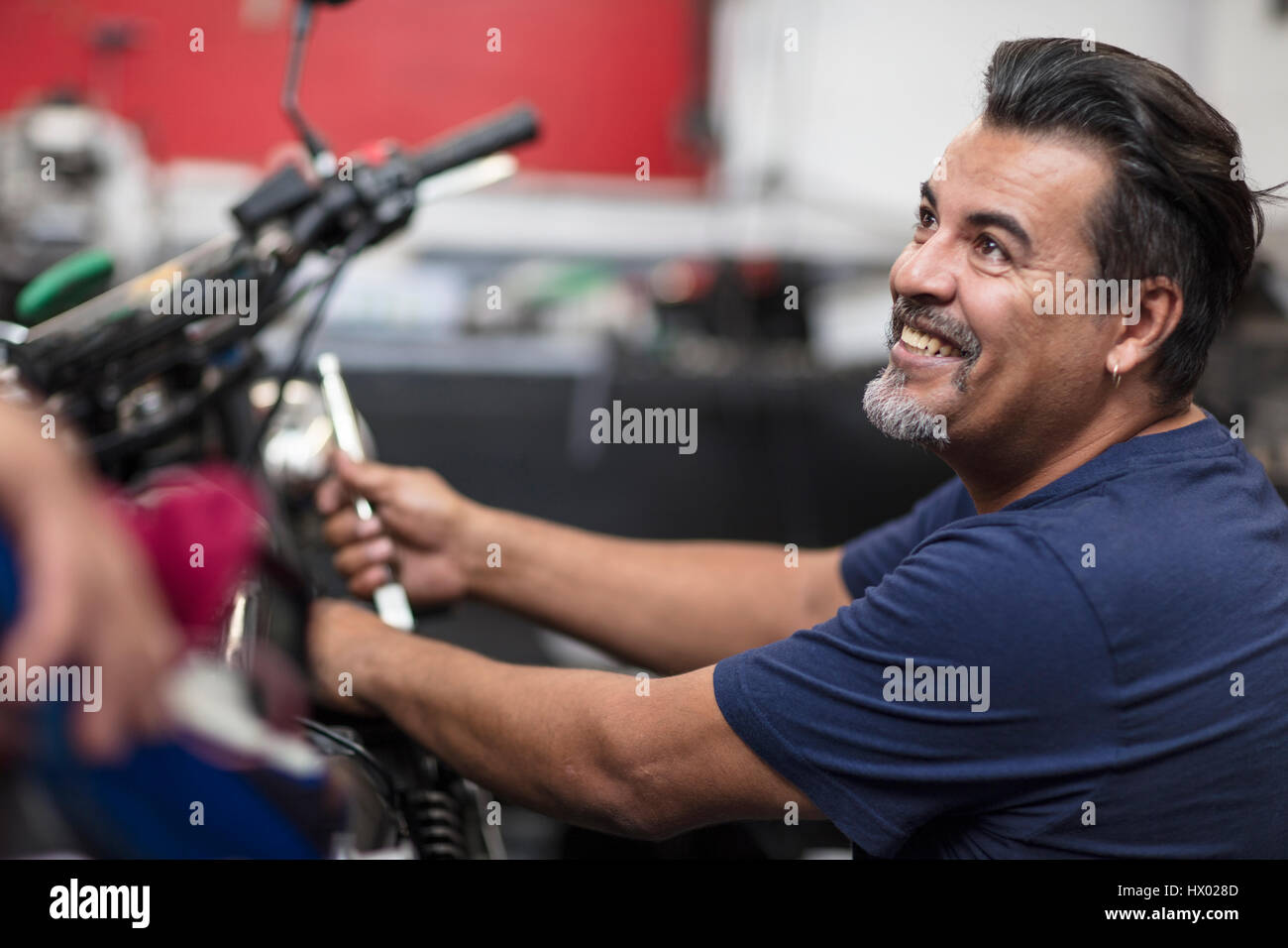 Smiling mechanic working on motorcycle in workshop Stock Photo - Alamy