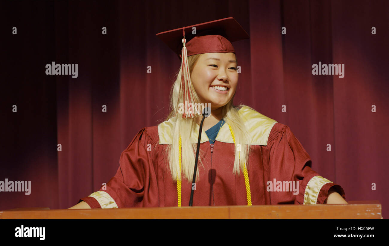 Smiling student speaking at podium on stage during graduation ceremony ...