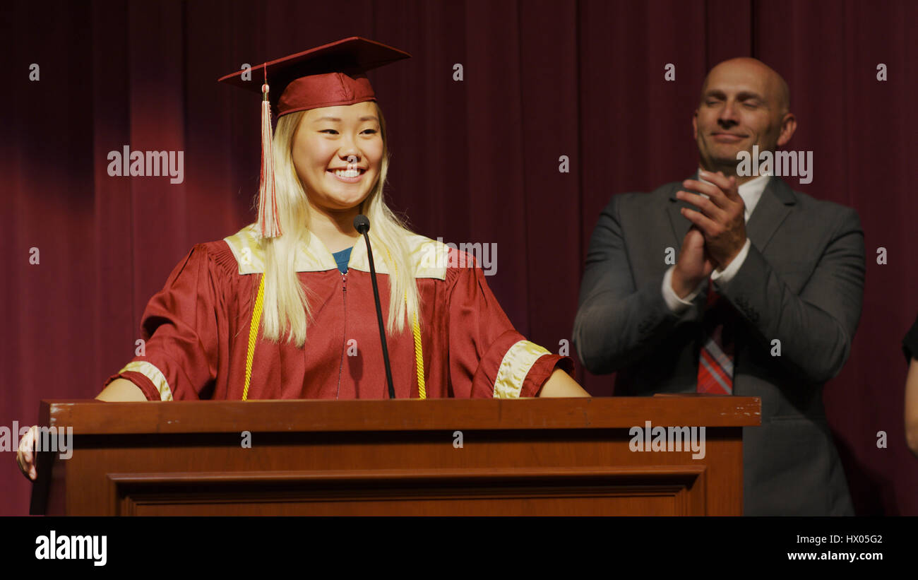 Teacher applauding smiling student speaking at podium on stage during ...
