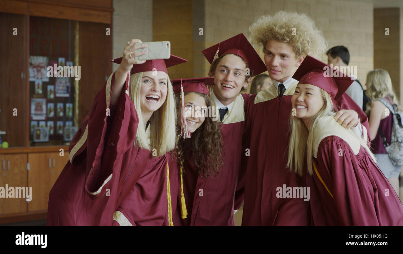 Smiling students taking smartphone camera selfie together at graduation ...