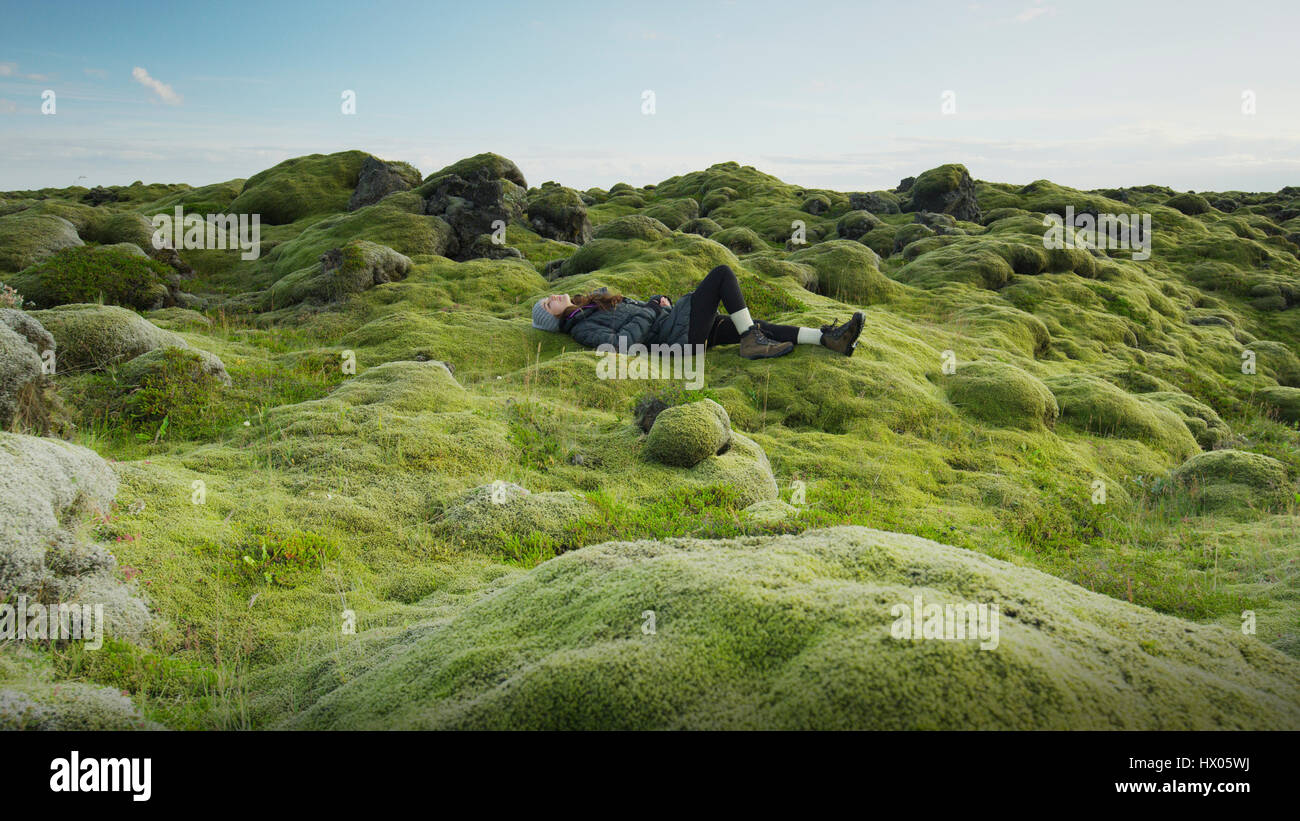 Side view of woman laying in mossy field in remote rocky landscape ...