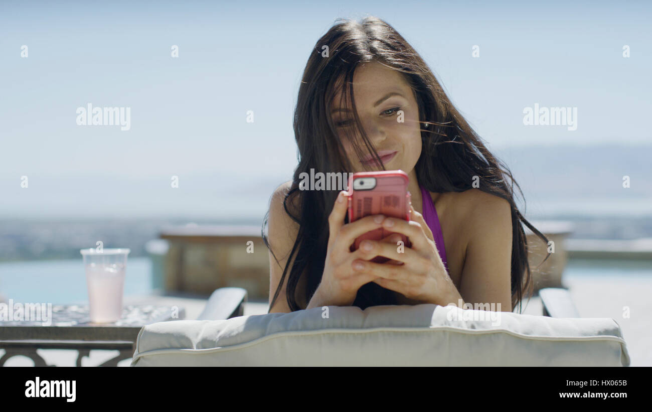 Close up of woman in bikini using cell phone and sunbathing on lawn chair near pool Stock Photo ...