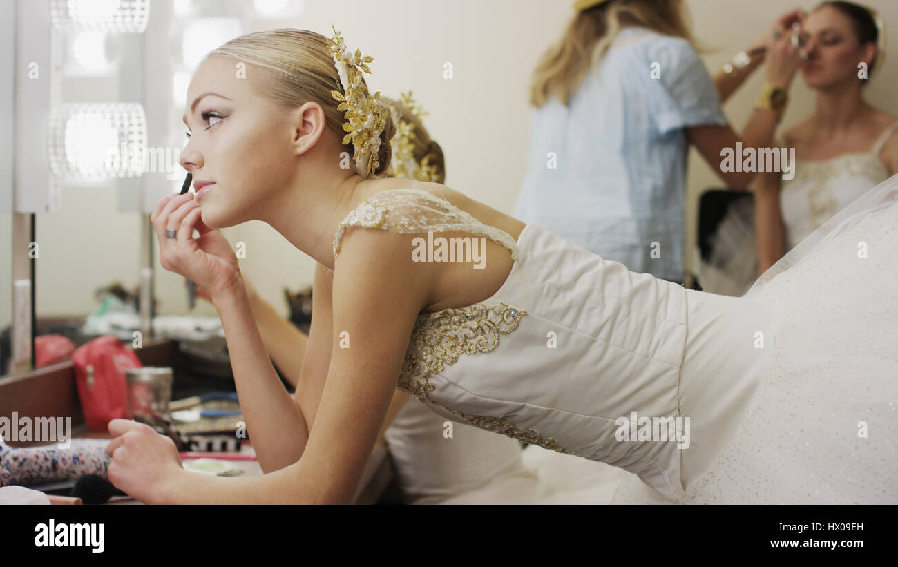 Profile of serious ballet dancer in costume applying makeup backstage ...