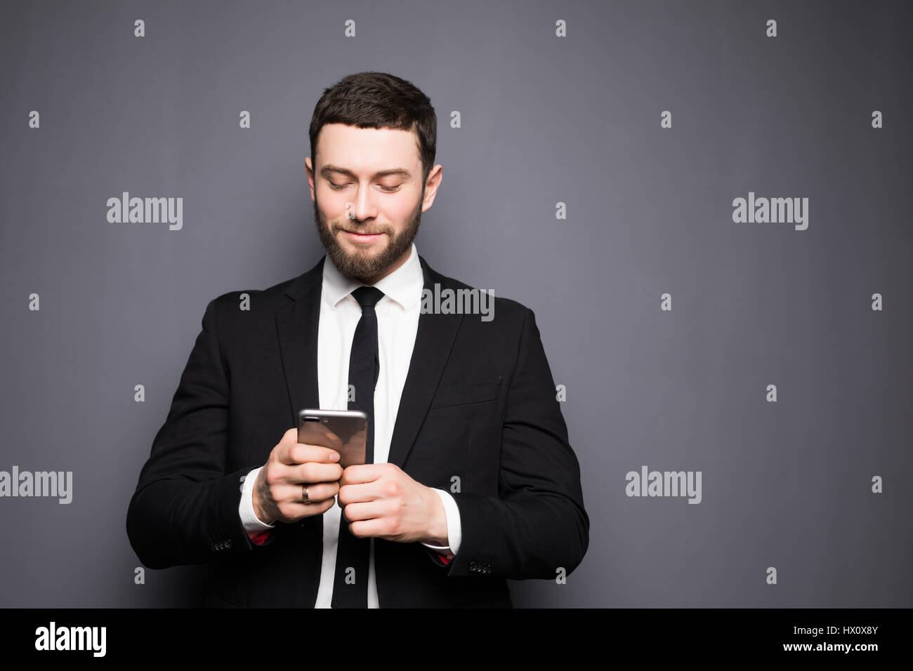 Handsome stylish young man writing sms on phone on dark background ...