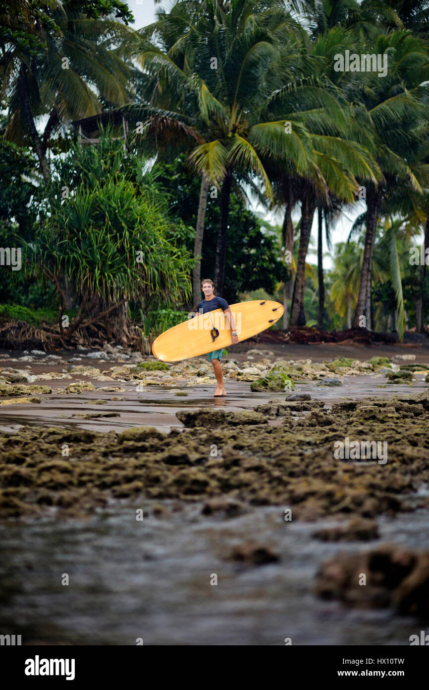 Indonesia, Java, man carrying surfboard at the coast Stock Photo - Alamy