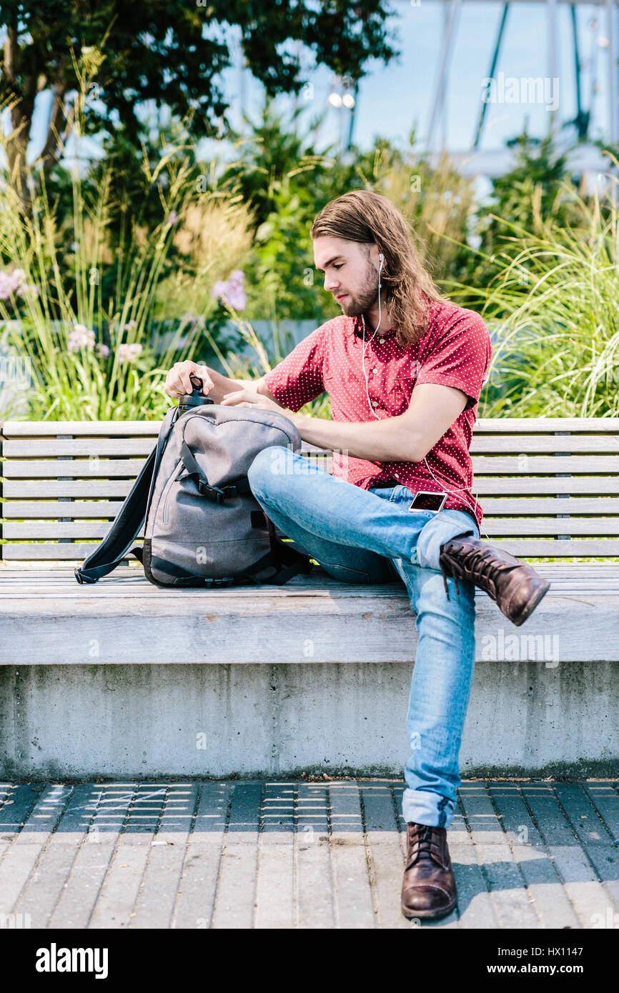 Man sitting on a bench with earbuds and backpack Stock Photo - Alamy