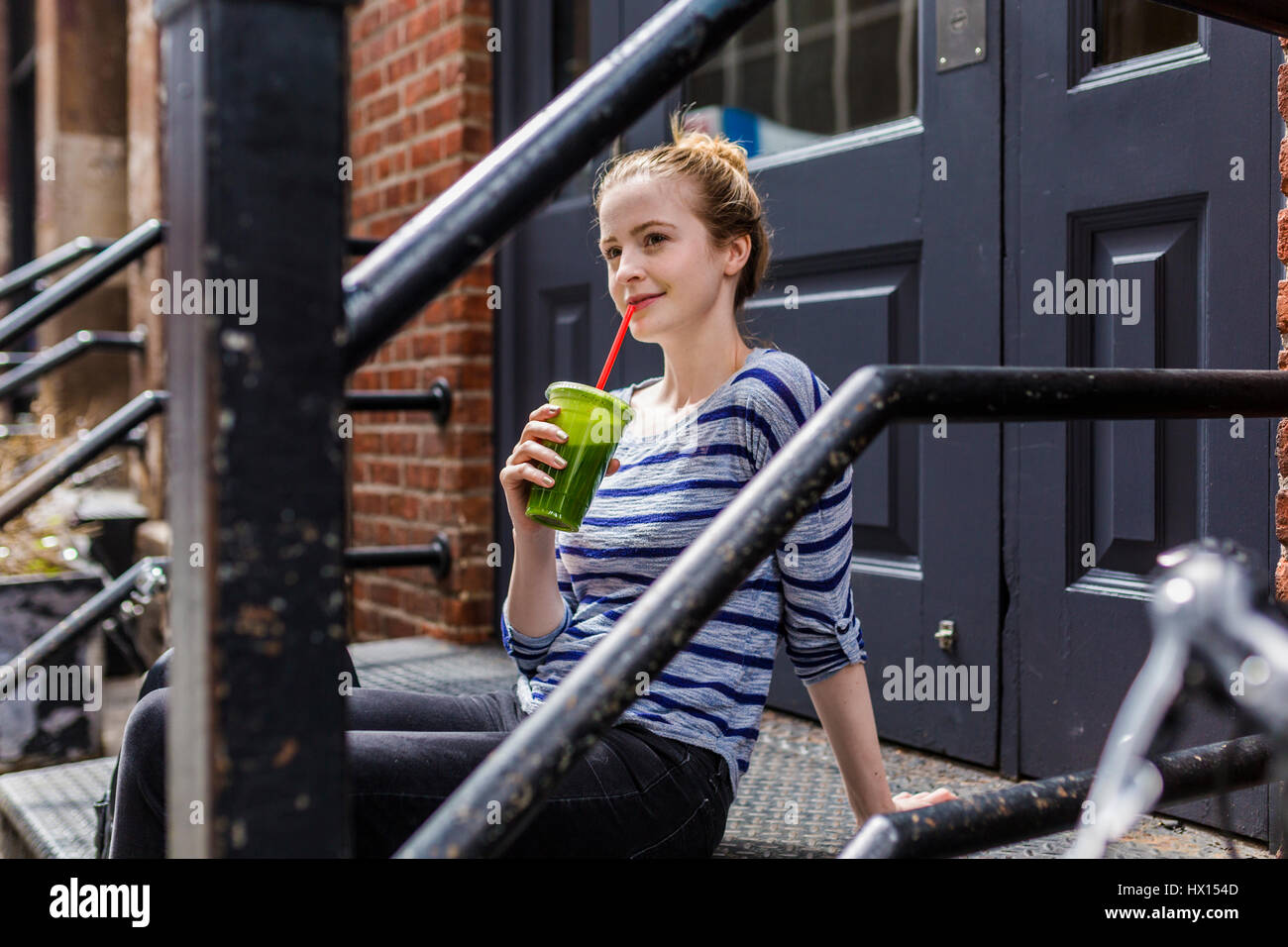 USA, New York City, woman sitting on stoop drinking a smoothie in ...