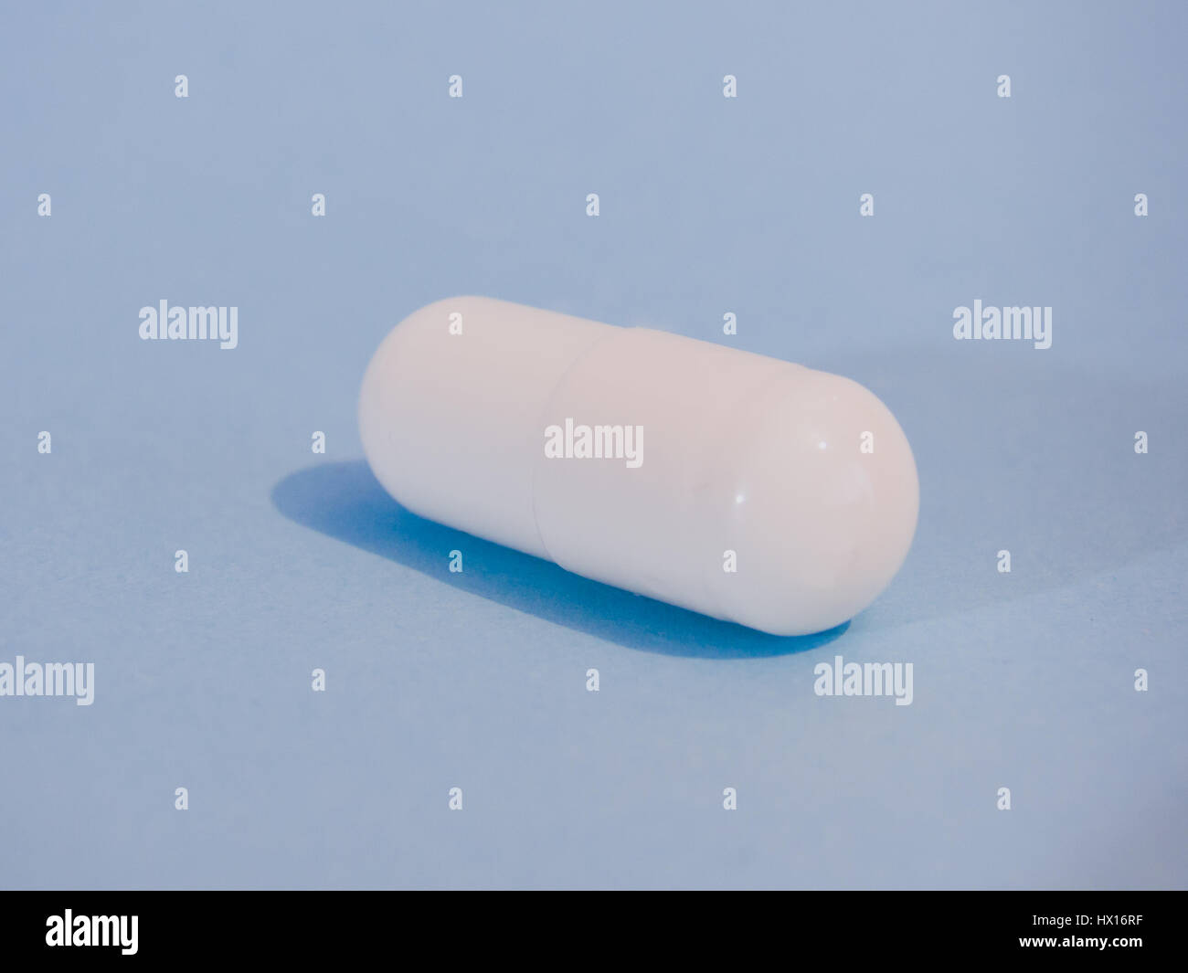 Large white hard capsule lying on a blue pastel background. Real shadow ...