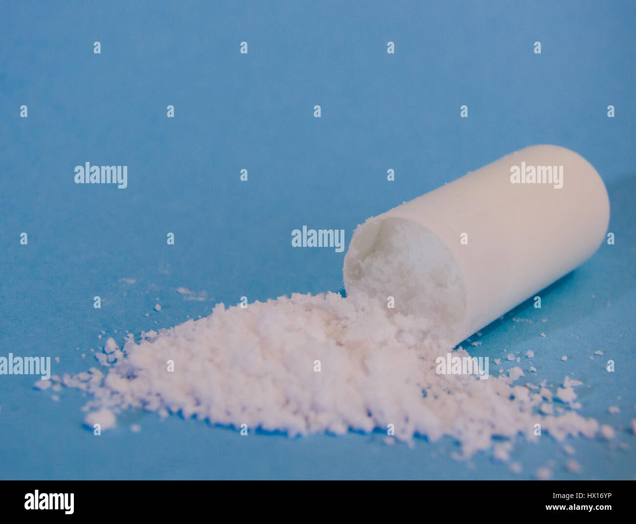 Large open white hard capsule with medicine falling out of it lying on ...