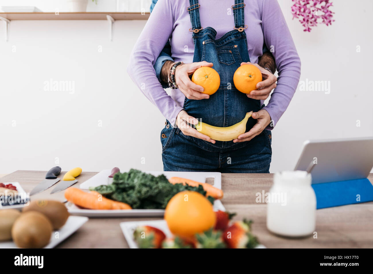 Expectant parents building smiley face on her belly with two oranges ...