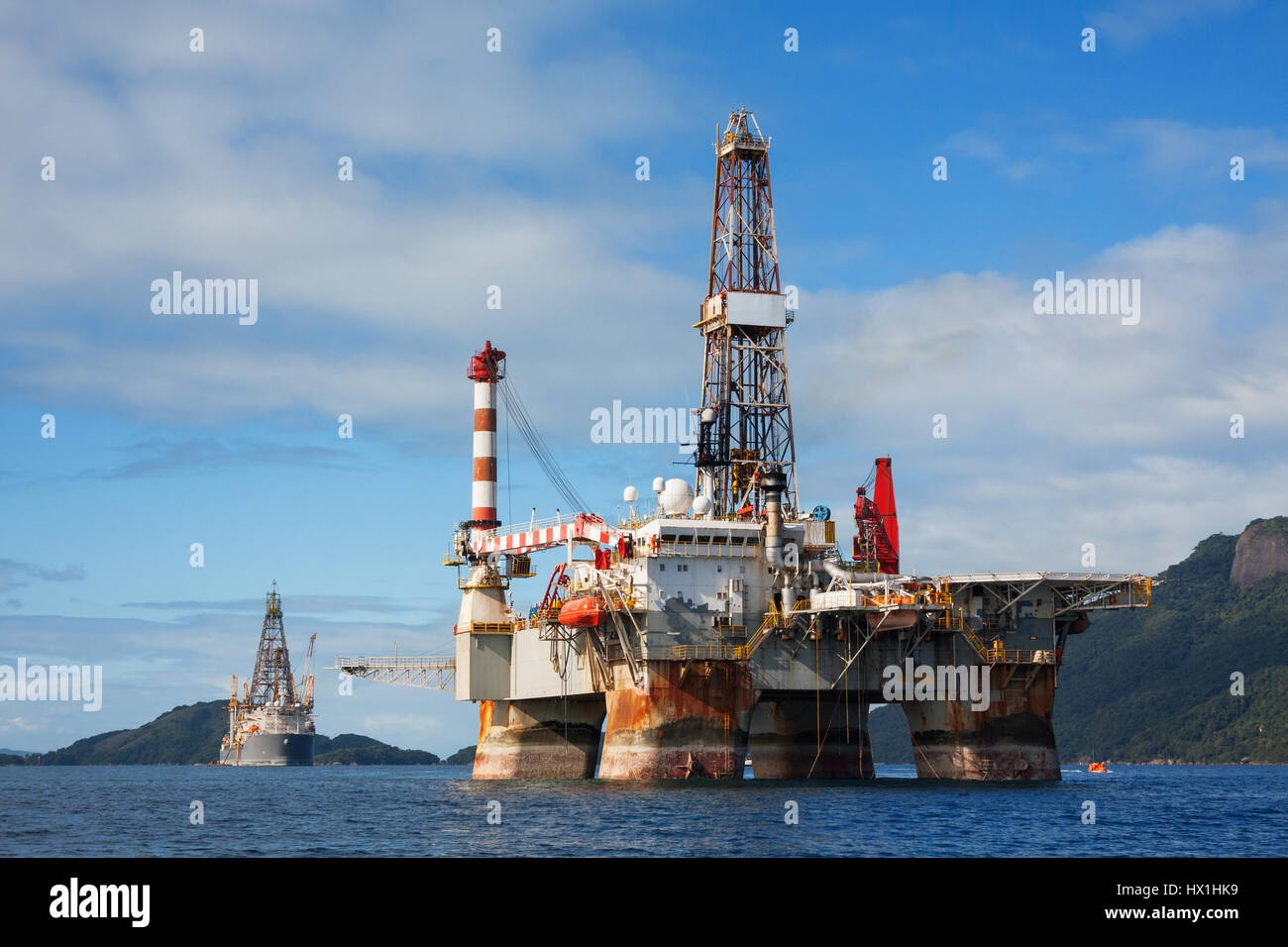 Offshore oil rig in front of green mountains with a blue sky above ...