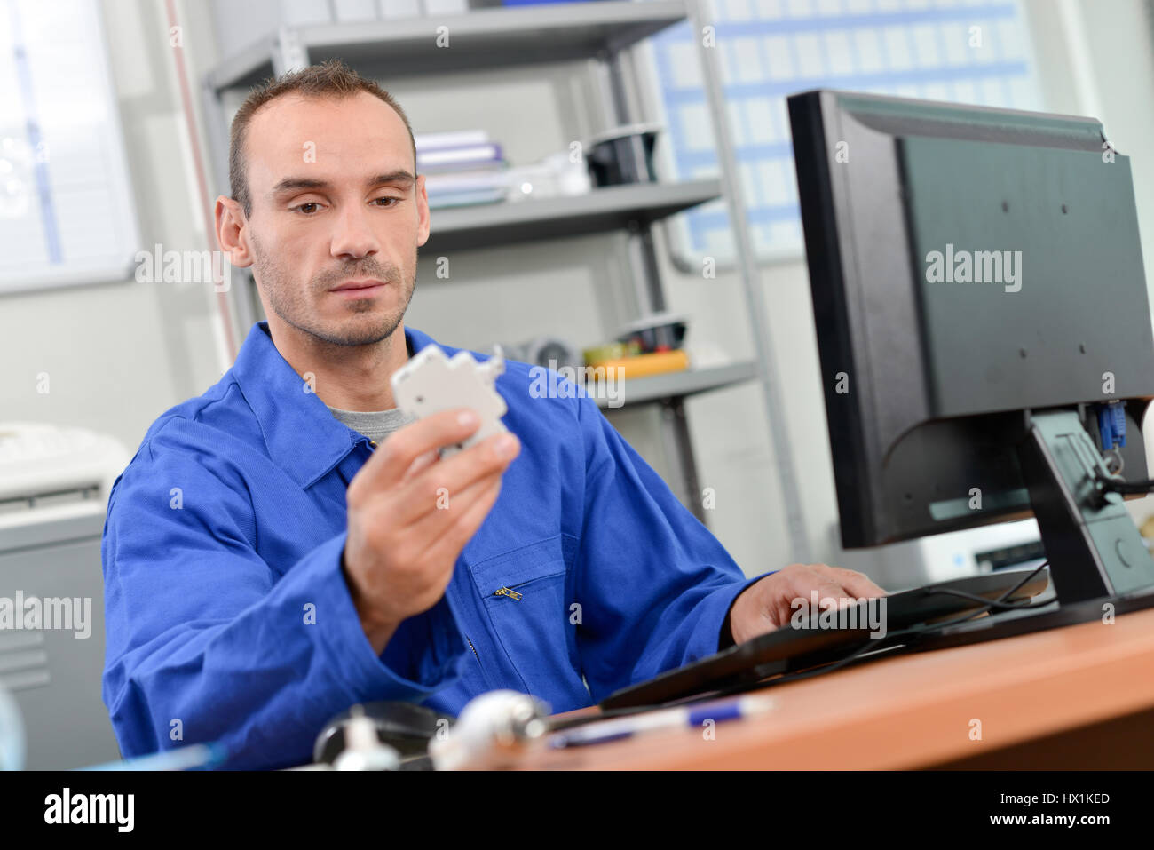 Man sat in front of computer, holding electrical component Stock Photo ...