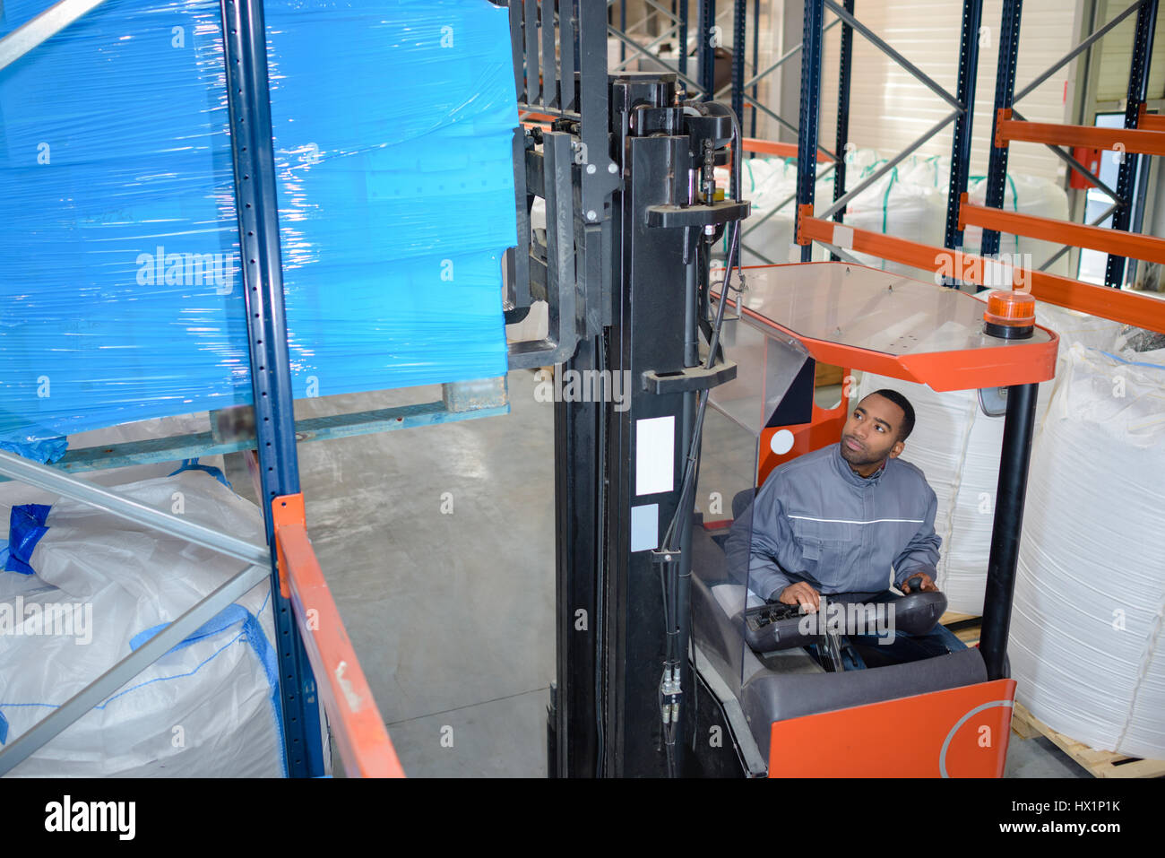 Forklift driver stacking pallet high in racking Stock Photo - Alamy
