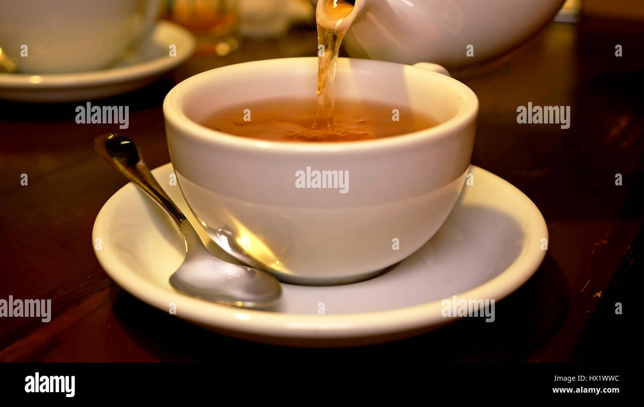 Pouring black tea into cup from teapot Stock Photo - Alamy