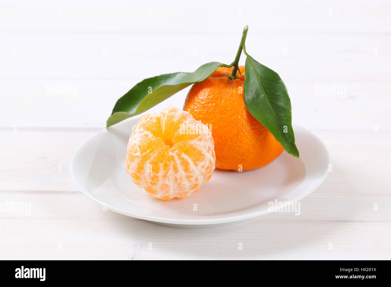 whole and peeled tangerines on white plate Stock Photo - Alamy