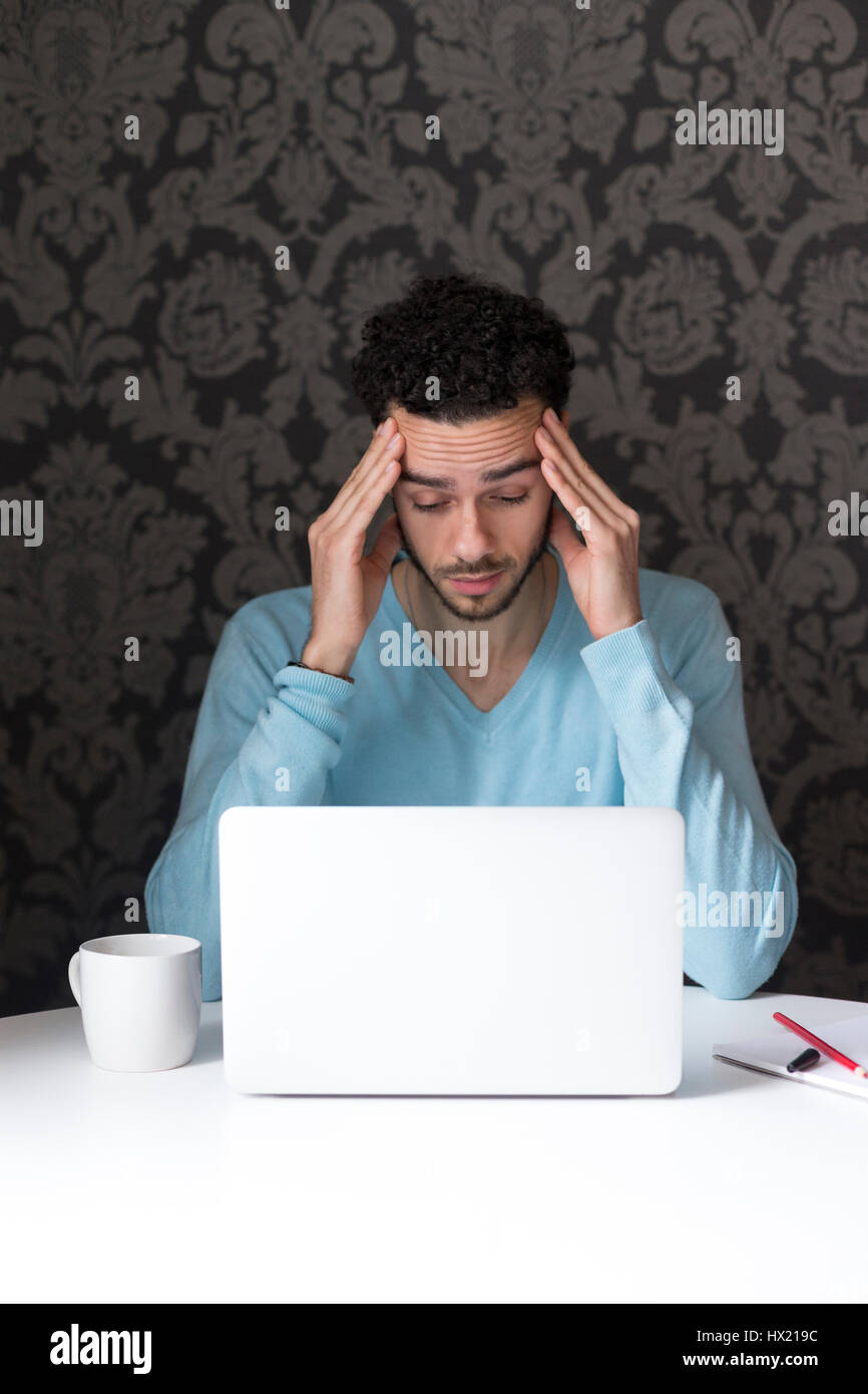 Stressed young man sitting at a computer with a cup of coffee. He has ...