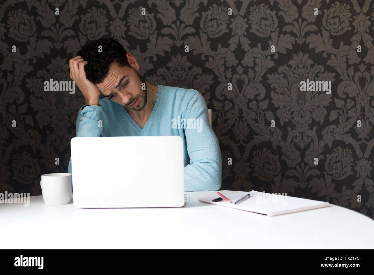 Stressed young man sitting at a computer with a cup of coffee. He has ...