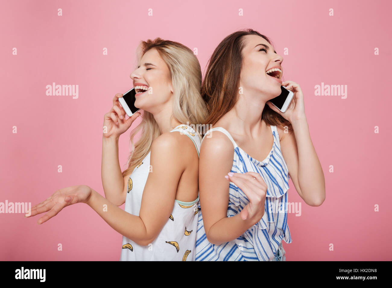 Two happy beautiful young women talking on mobile phones and laughing ...
