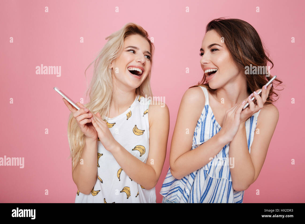 Two cheerful pretty young women using on cell phones and laughing over ...