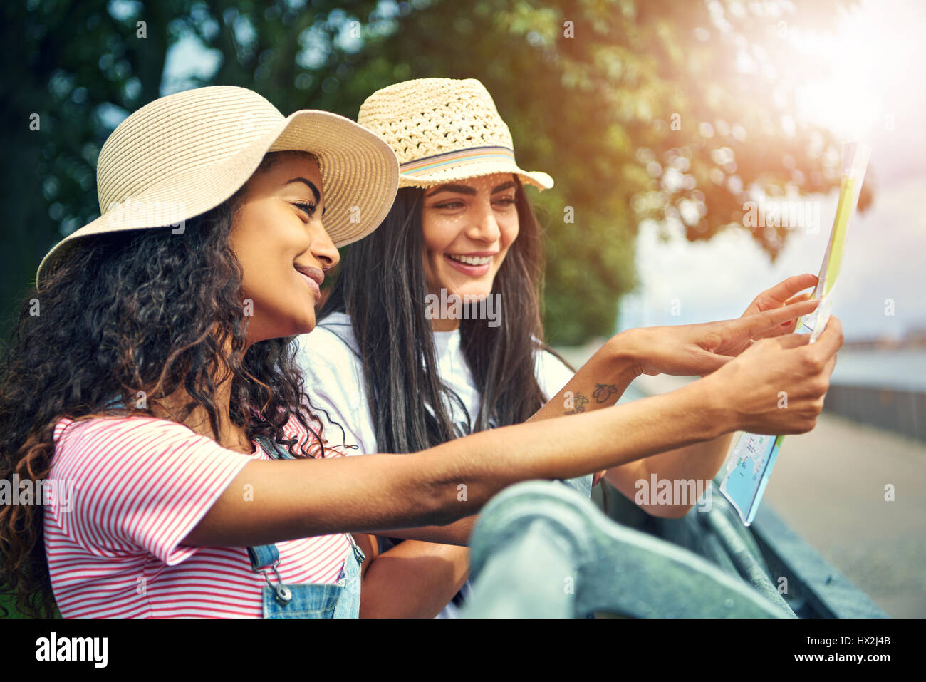 Two cute lady friends in straw hats smiling with their map in hand ...
