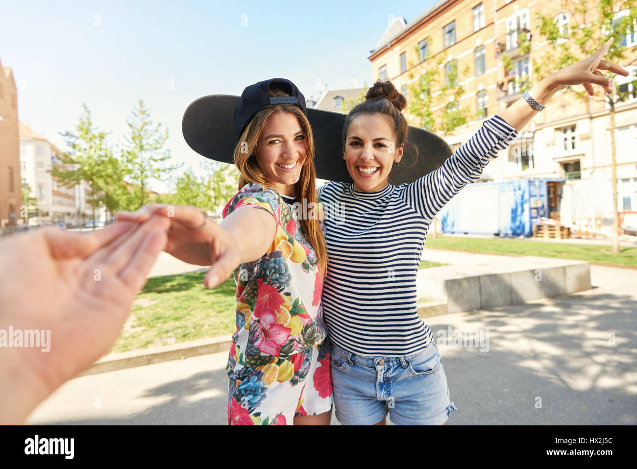 Smiling trendy woman standing arm in arm with her friend posing with ...
